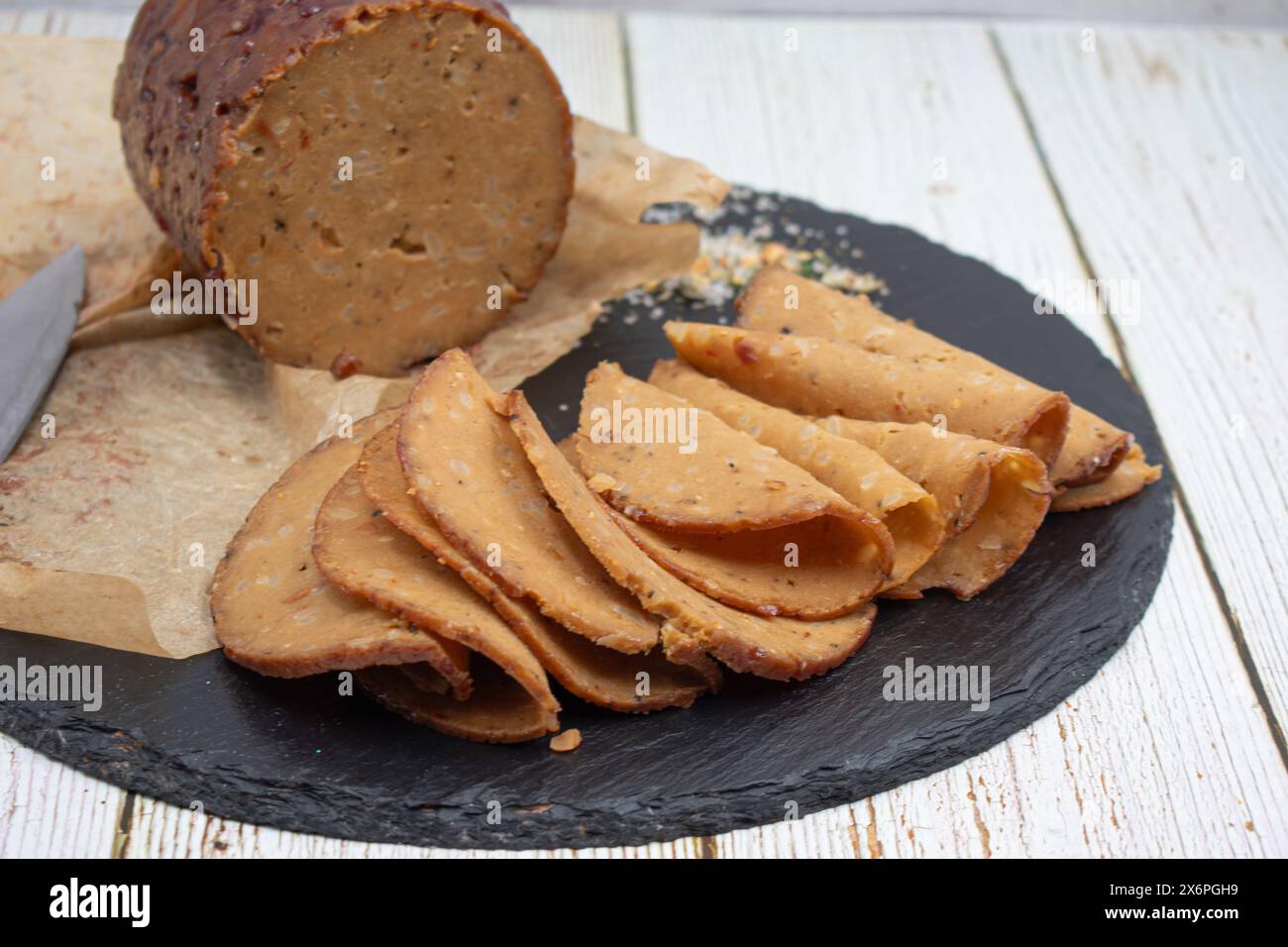 Seitan shaped and cooked in ham press, sliced on slate board. Vegan ...