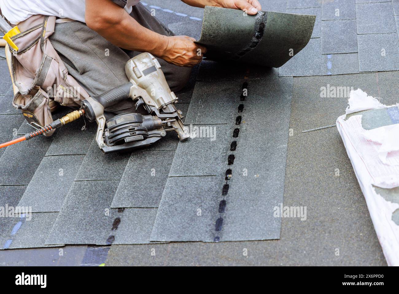 Roofer uses an air pneumatic nail gun to attach new asphalt bitumen ...