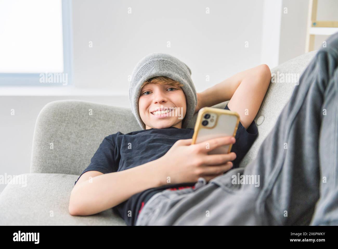 young boy lay on the couch at home watching cellphone wearing toque ...