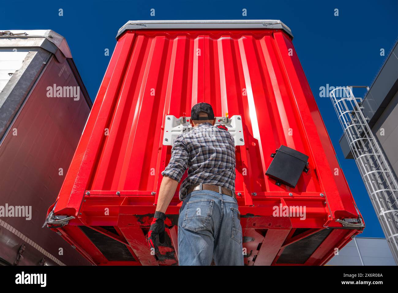 Semi truck driver performing maintenance on the rear of a red trailer ...