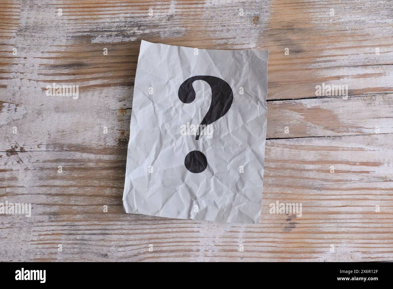 Gray crumpled paper note with question mark on it on a wooden ...