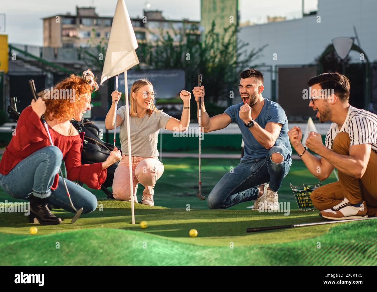 Group of smiling friends enjoying together playing mini golf in the ...