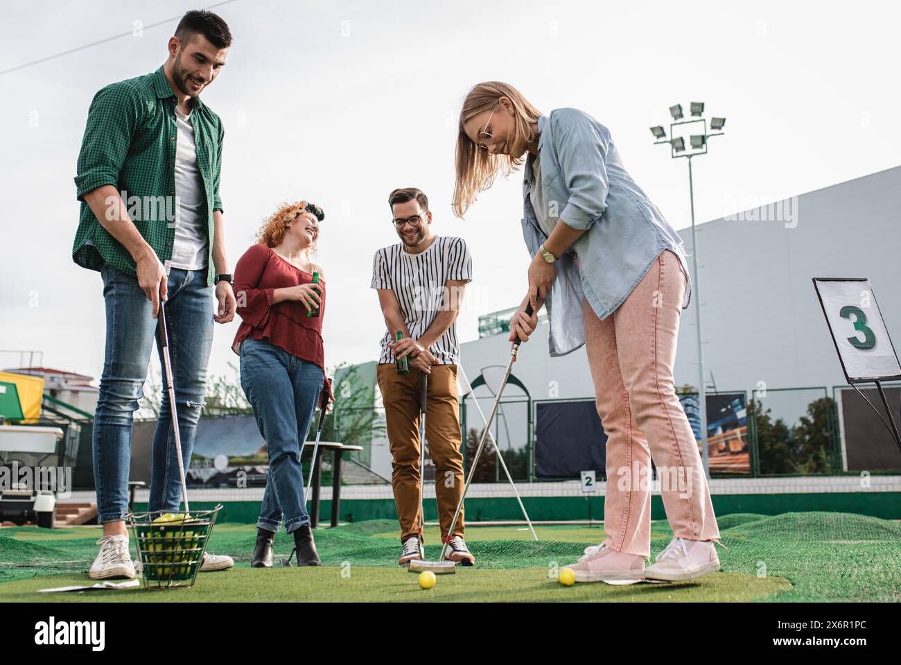 Group of smiling friends enjoying together playing mini golf in the ...