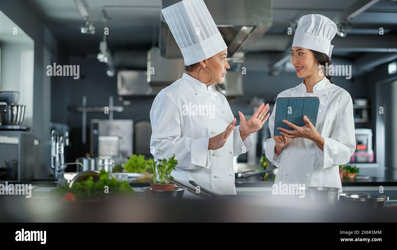 Restaurant Kitchen: Team of Asian and Black Female Chefs use Tablet ...