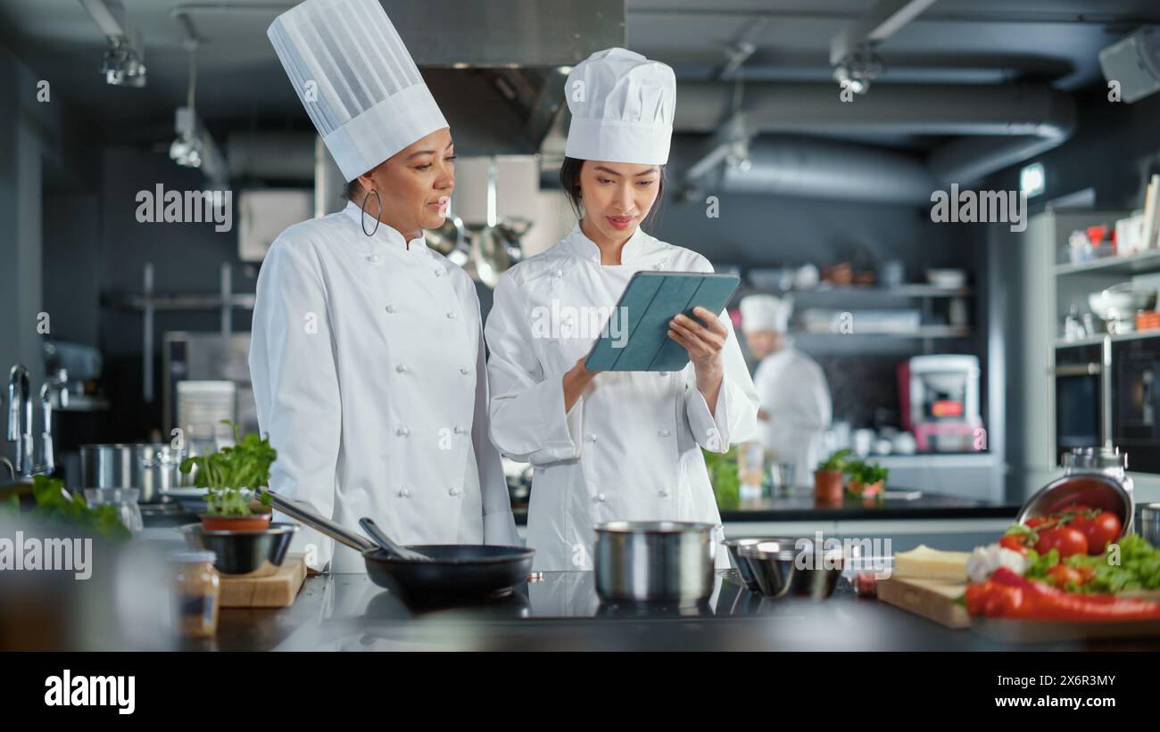 Restaurant Kitchen: Team of Asian and Black Female Chefs use Tablet ...