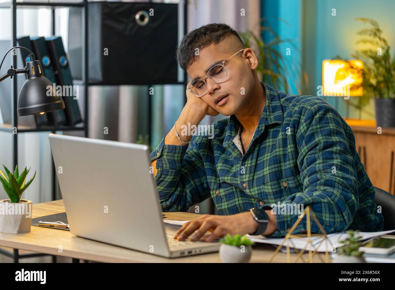 Bored sleepy Indian businessman worker working on laptop computer yawns ...
