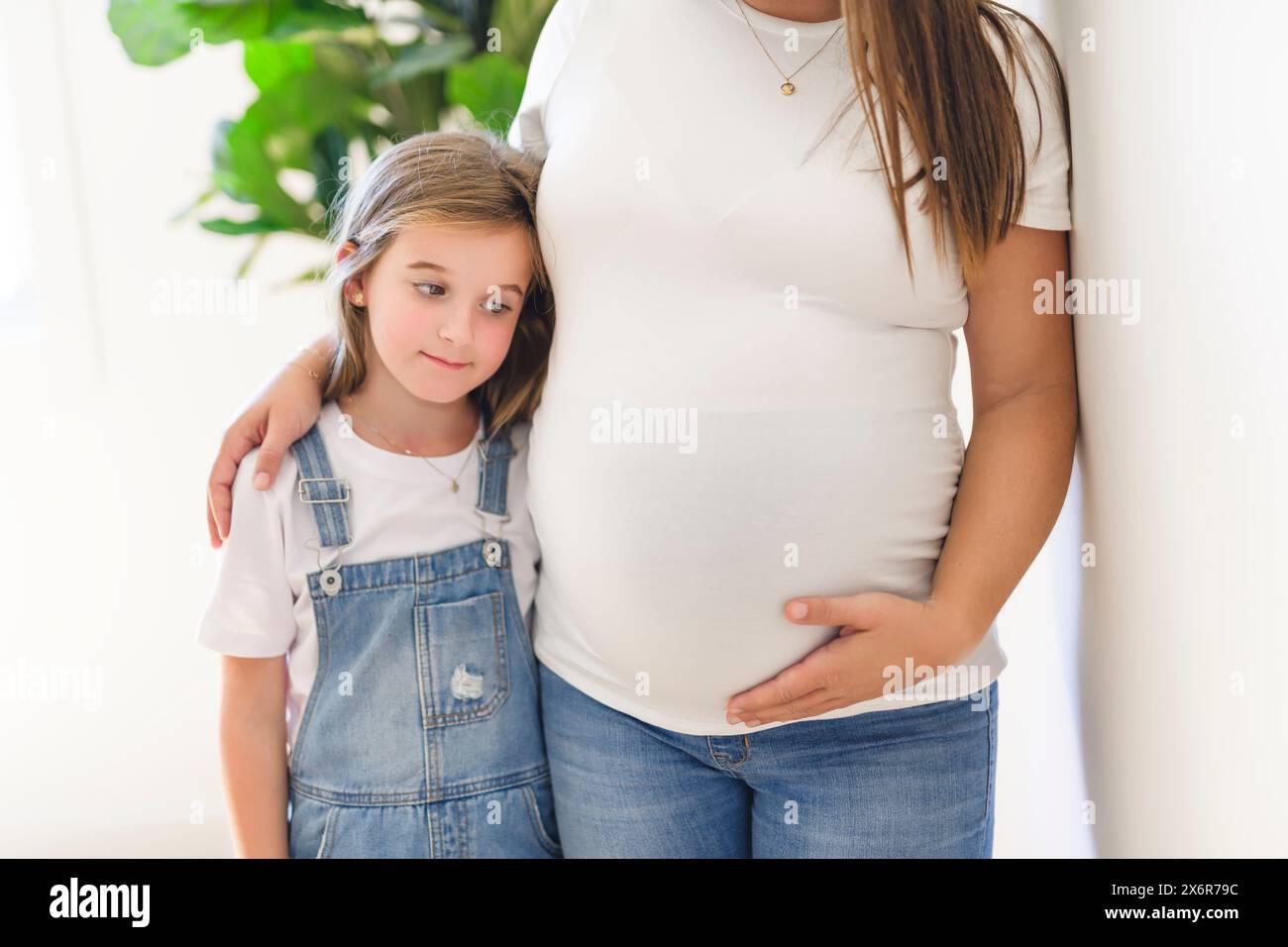Excited little daughter touching pregnant mom tummy, standing next to ...