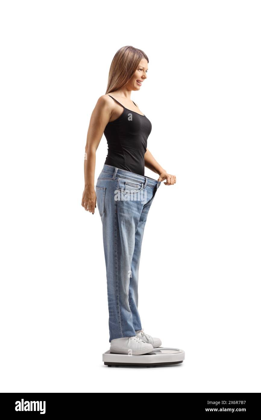 Woman wearing a big size jeans and weighing on a medical scale isolated ...