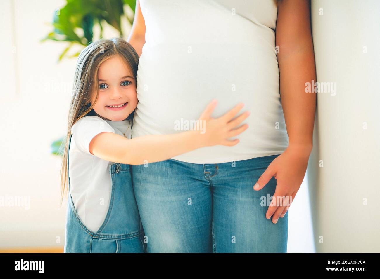 Excited little daughter touching pregnant mom tummy, standing next to ...