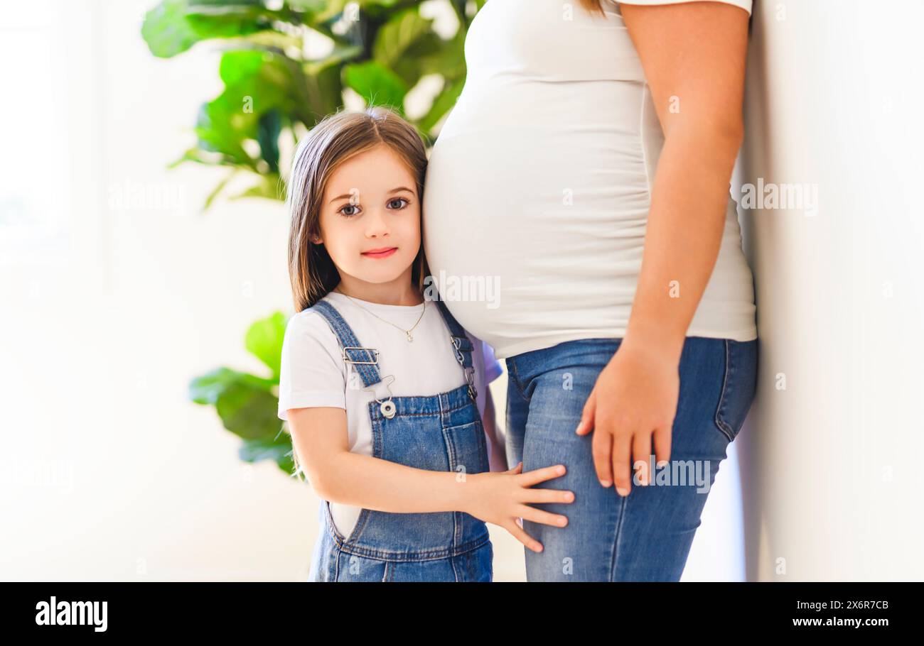 Excited little daughter touching pregnant mom tummy, standing next to ...