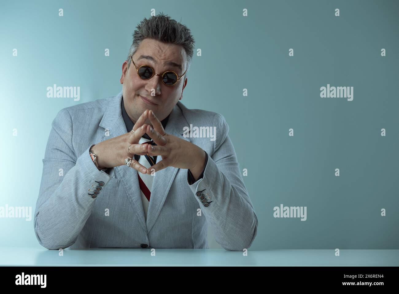 Businessman in grey suit smirks confidently behind desk, fingers ...