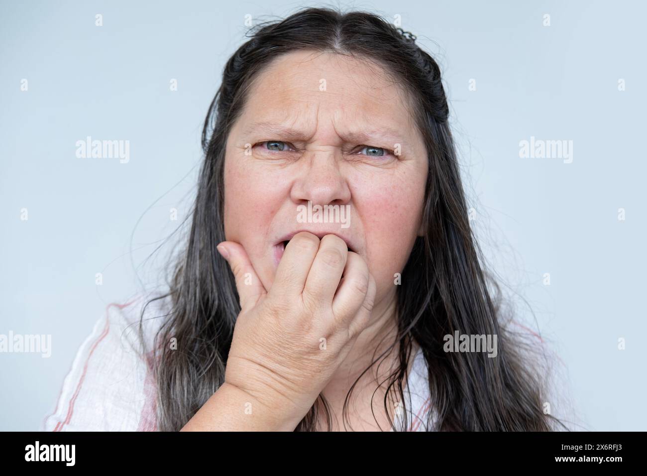 distressed mature woman with long hair nervously biting her nails ...