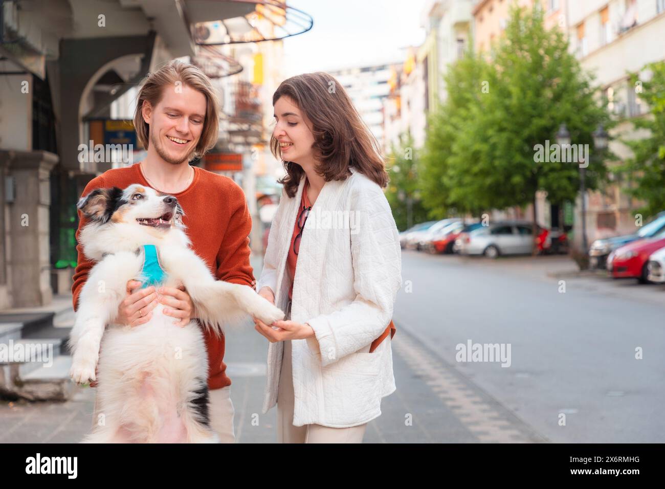 Happy young couple, man and woman hugs their dog Aussie at the street ...