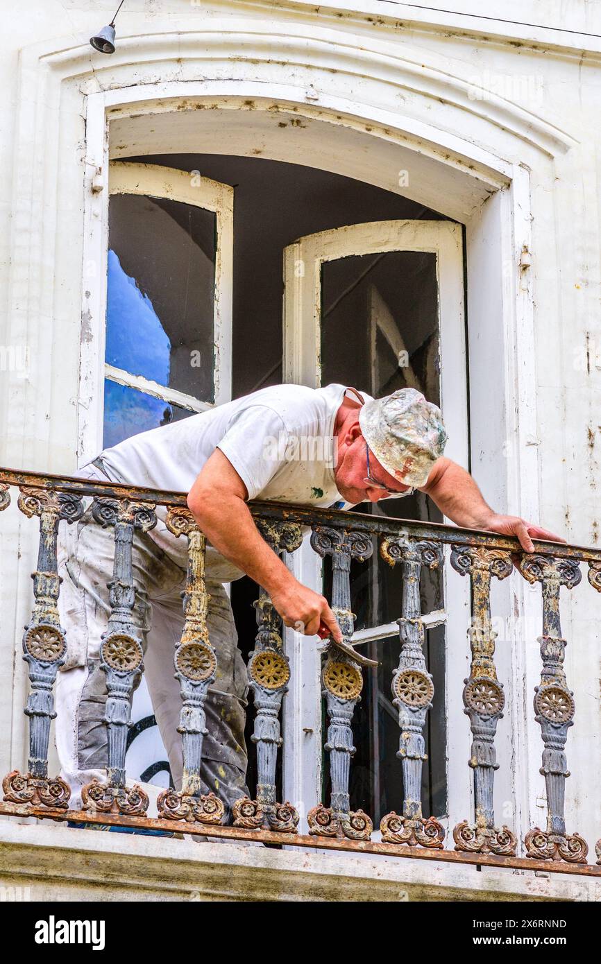 Workman using wire brush to scrape loose paint and rust from balcony ...