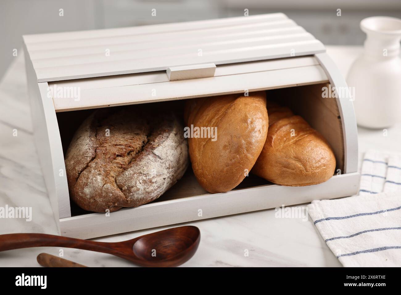Wooden bread basket with freshly baked loaves and spoons on white ...