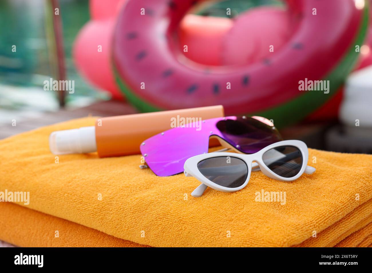 Beach towels, sunglasses and sunscreen on sunbed near outdoor swimming ...