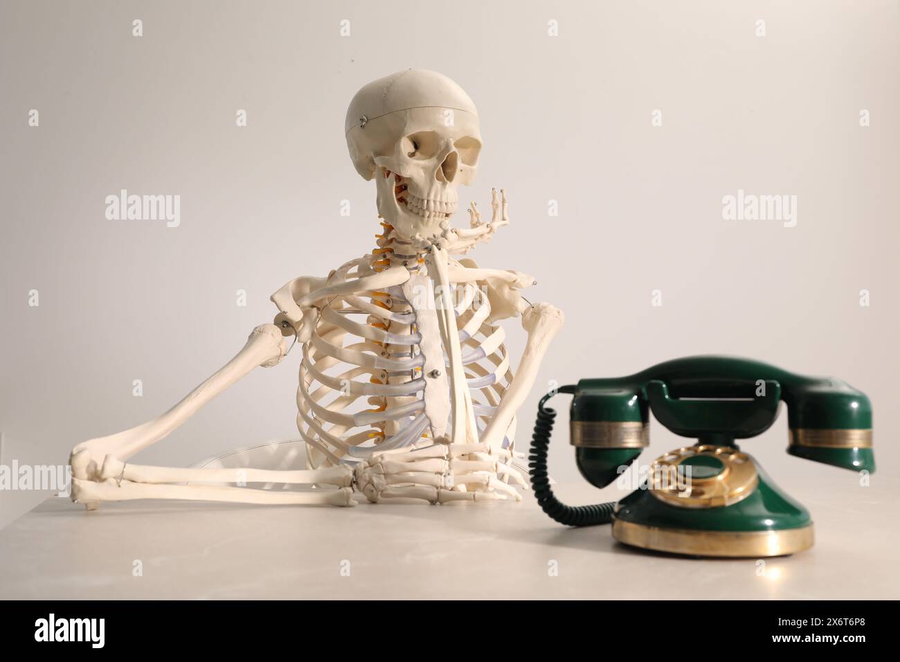 Waiting concept. Human skeleton at table with corded telephone against ...