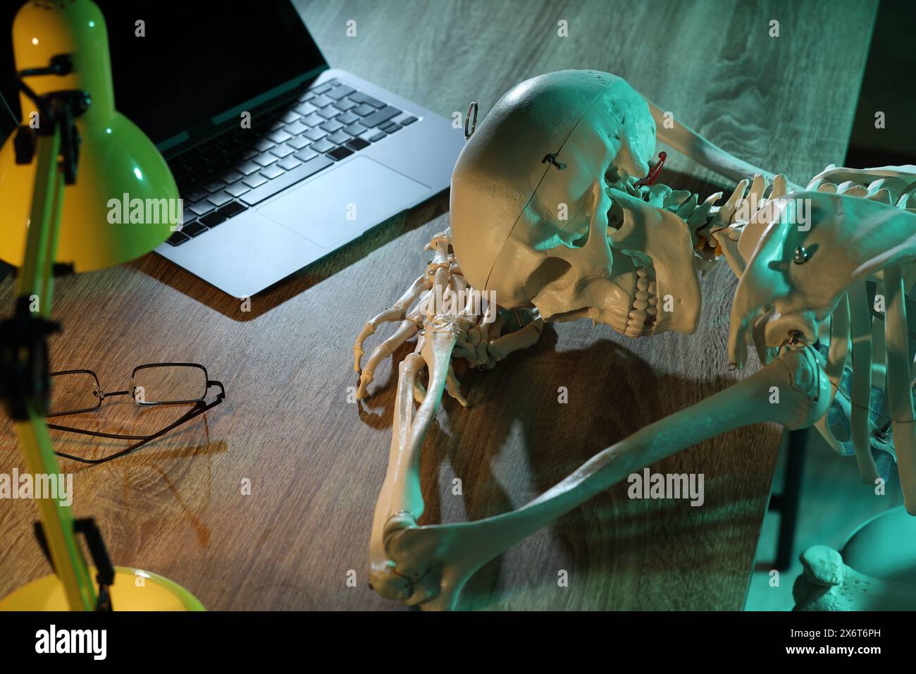 Waiting concept. Human skeleton sleeping at wooden table with laptop ...