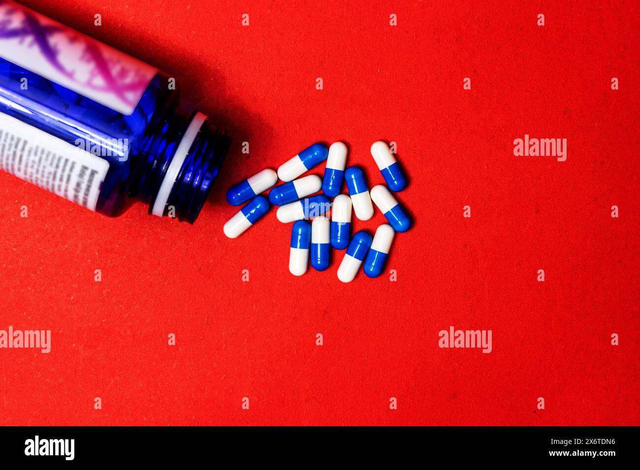 blue and white medicinal pill capsules on a bright red background ...