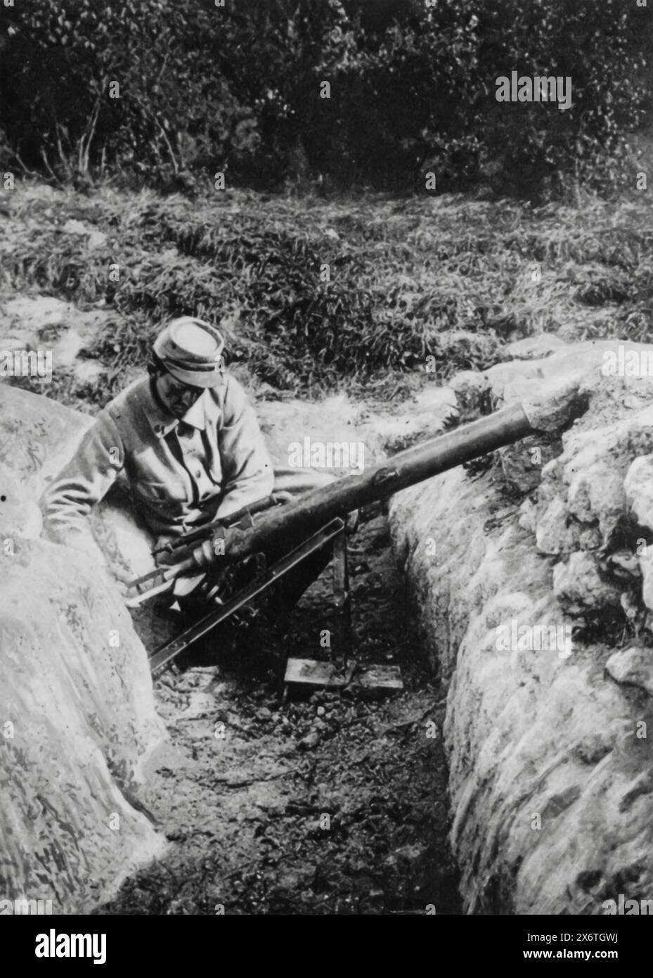 A photograph of a French soldier in a shallow trench reloading a mortar ...