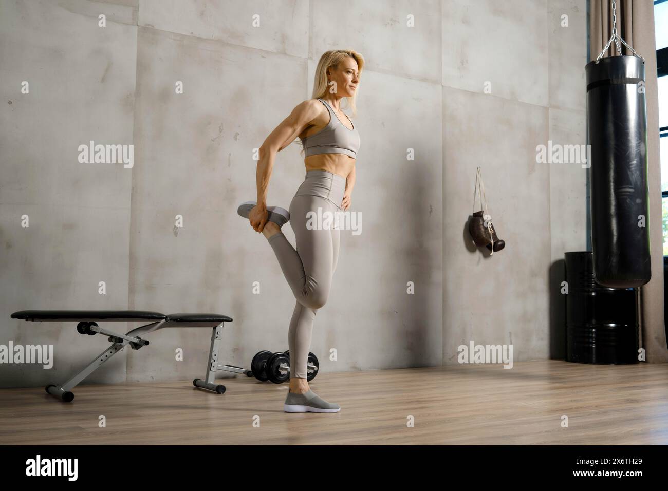 Active blonde woman stretching leg before workout and fitness in gym ...