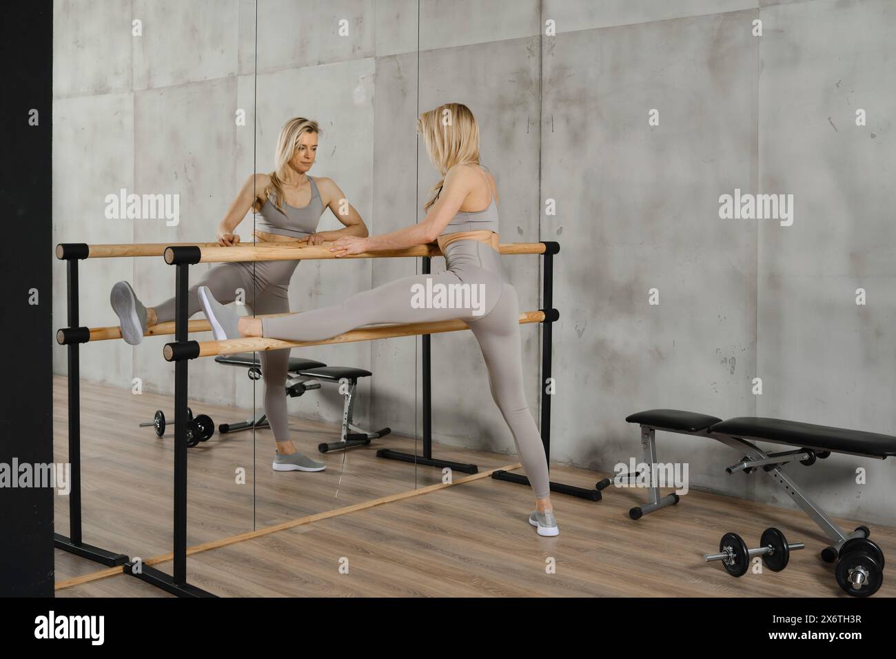 Fitness athlete standing in front of a wall mirror and stretching leg ...
