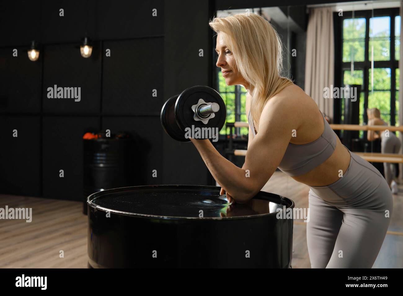 Side view of middle-aged woman pushing dumbbell in the gym leaning on ...