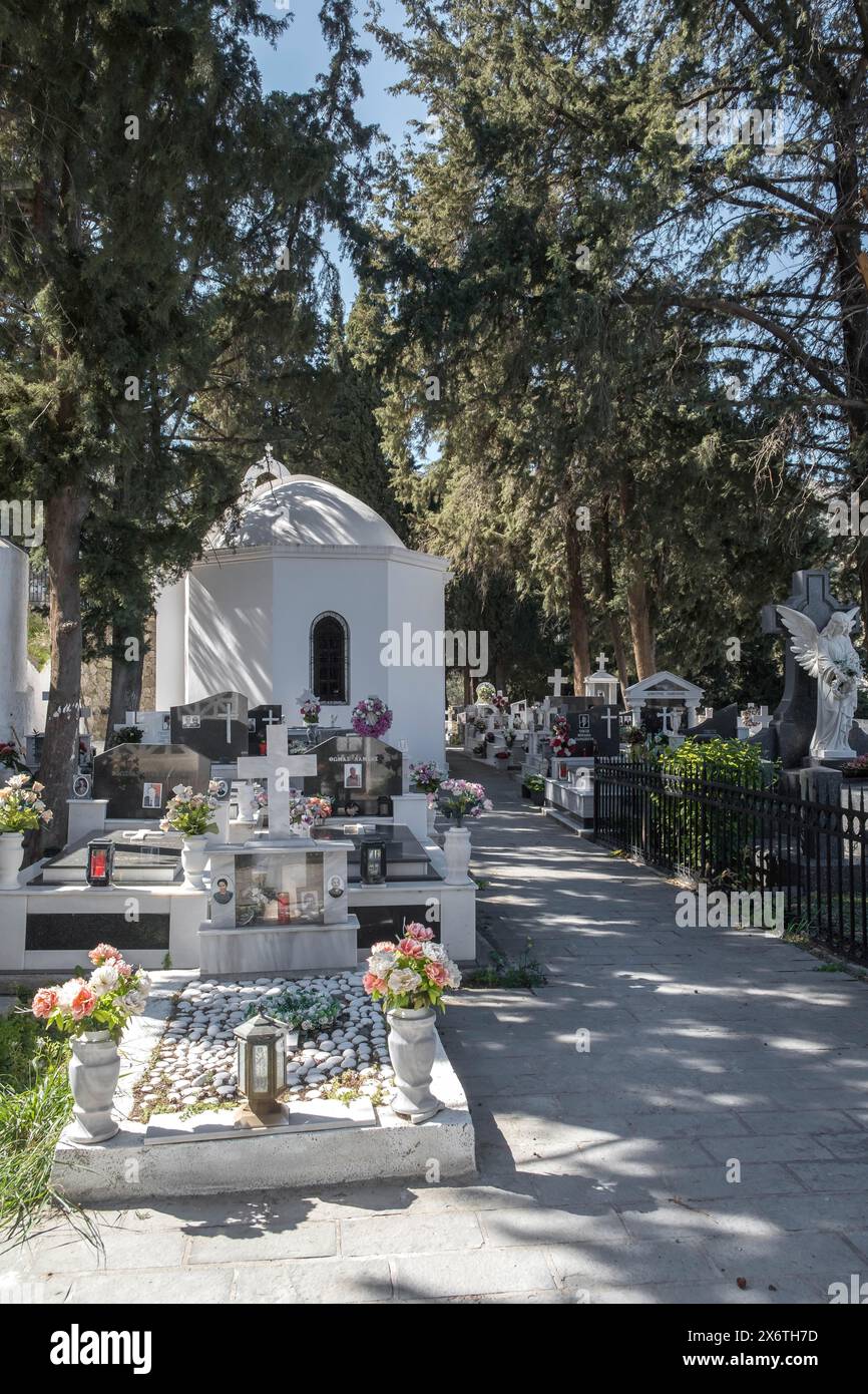 A white chapel surrounded by tombstones and an angel statue in a ...