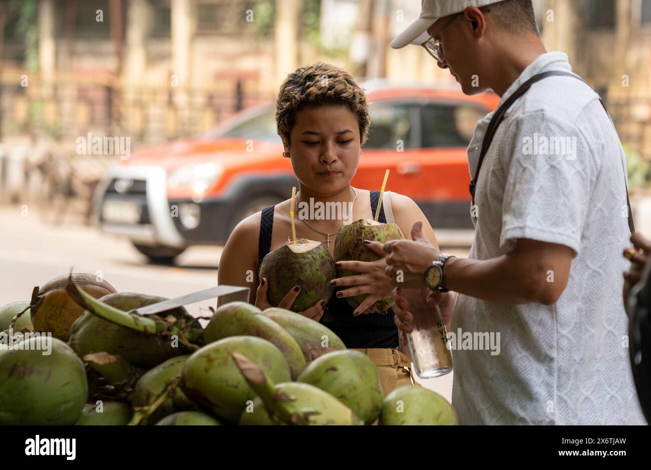 People drink coconut water along the roadside on a hot summer day, in ...