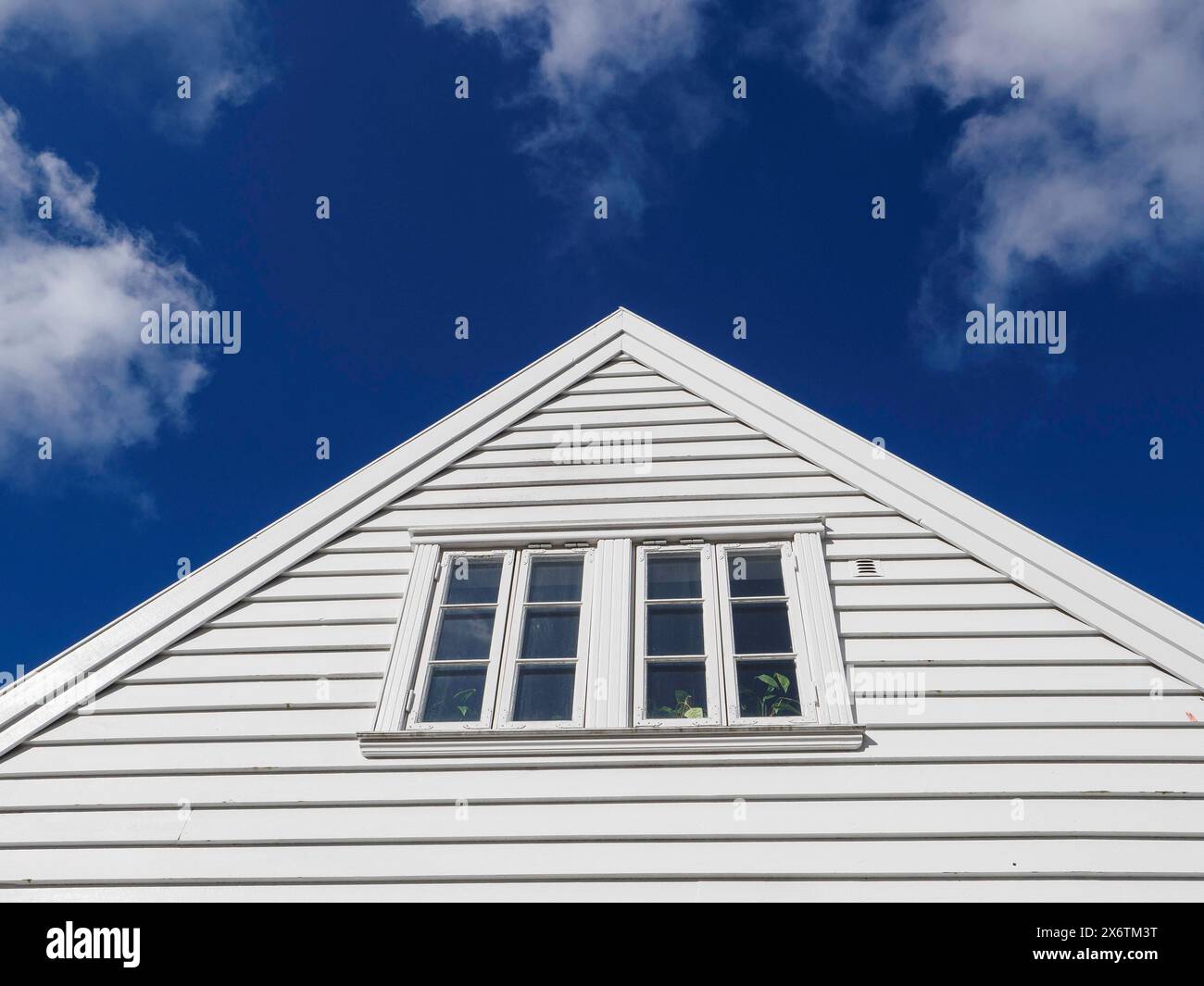 White wooden house with a window in a triangular gable in front of a ...