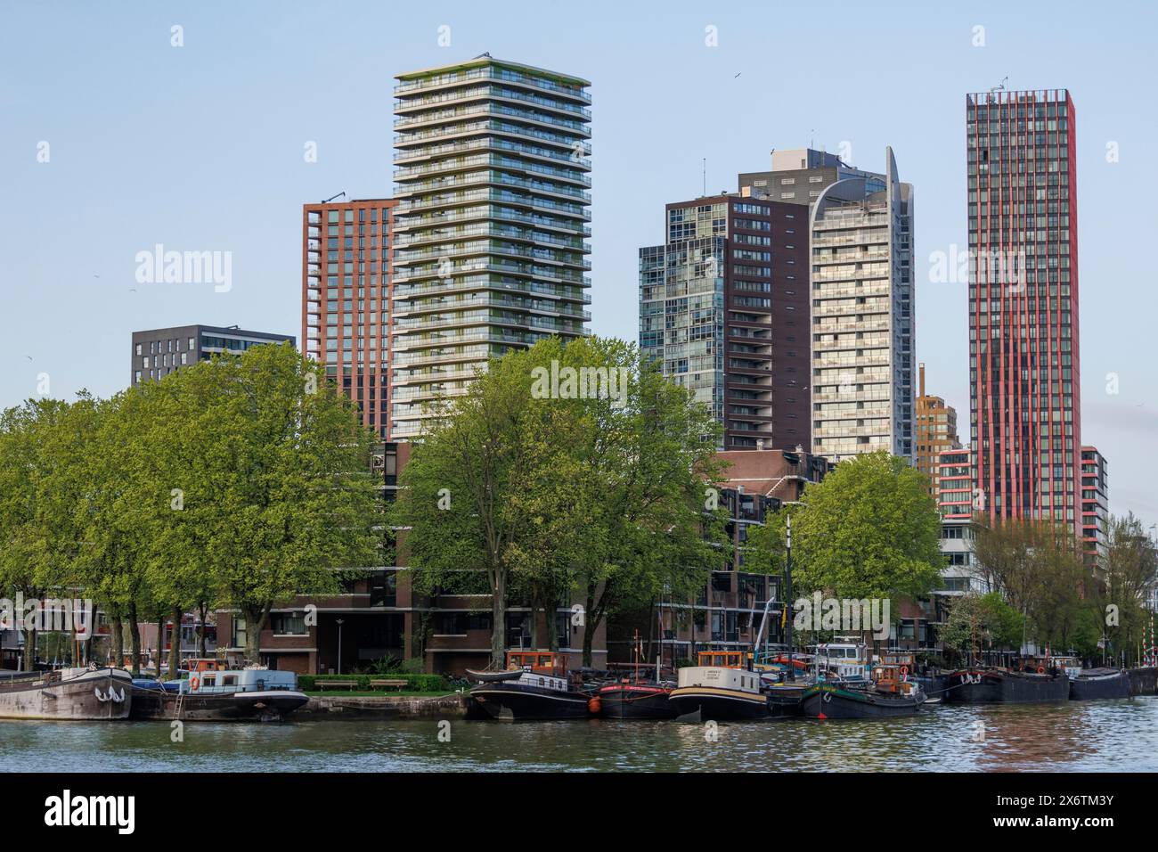 Modern high-rise buildings along a river, surrounded by green trees and ...