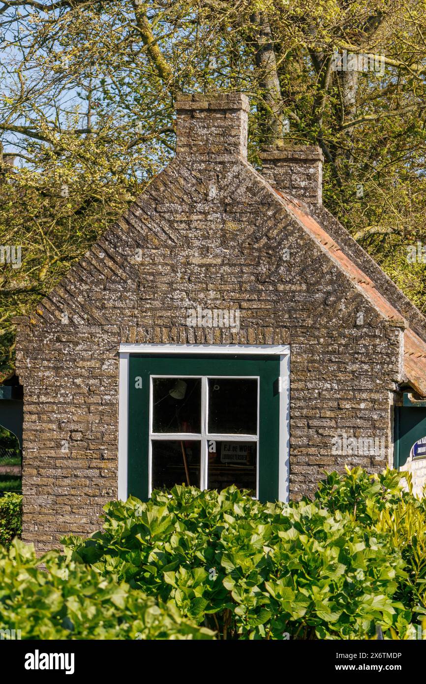 A small, rustic stone house with one window, surrounded by green bushes ...