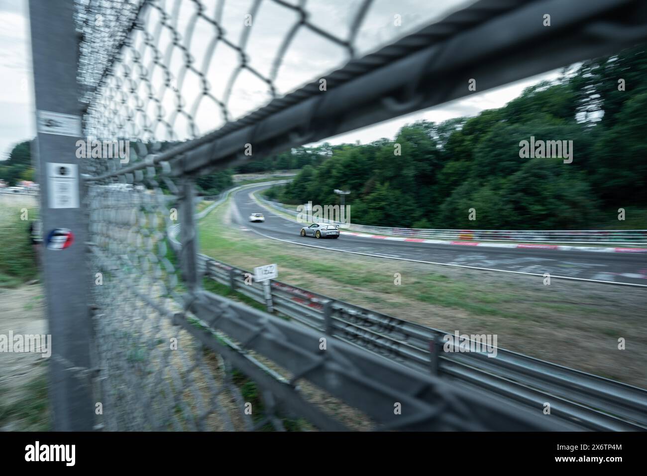 Cars race past on a race track, seen through a safety fence ...
