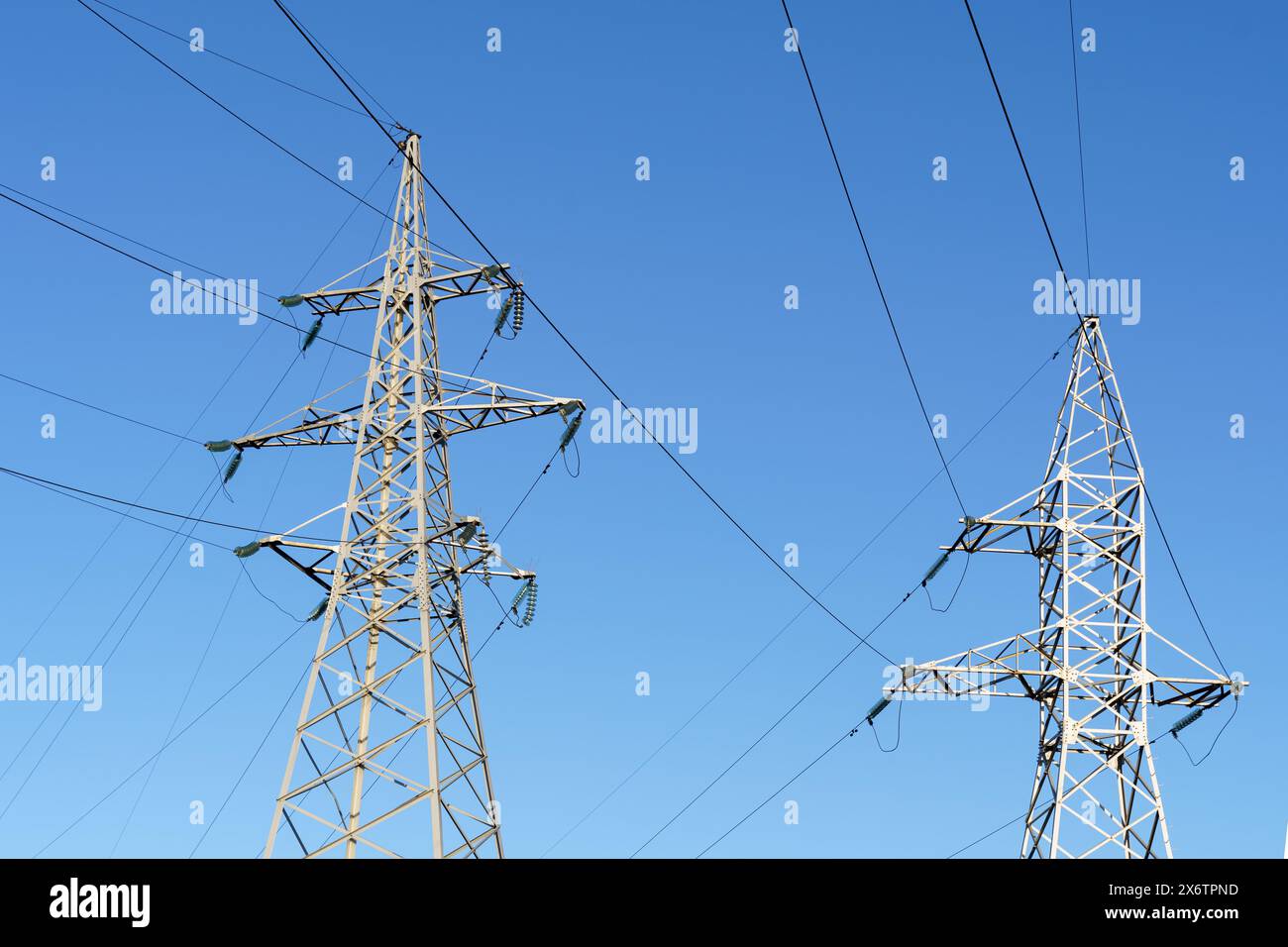 High voltage pylons stand tall against a clear blue sky, carrying ...