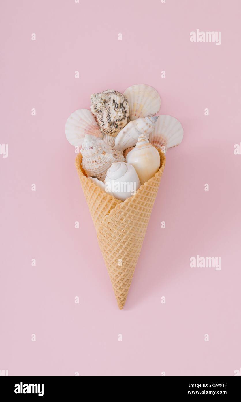 Ice cream cone with various sea shells on light pastel pink background ...
