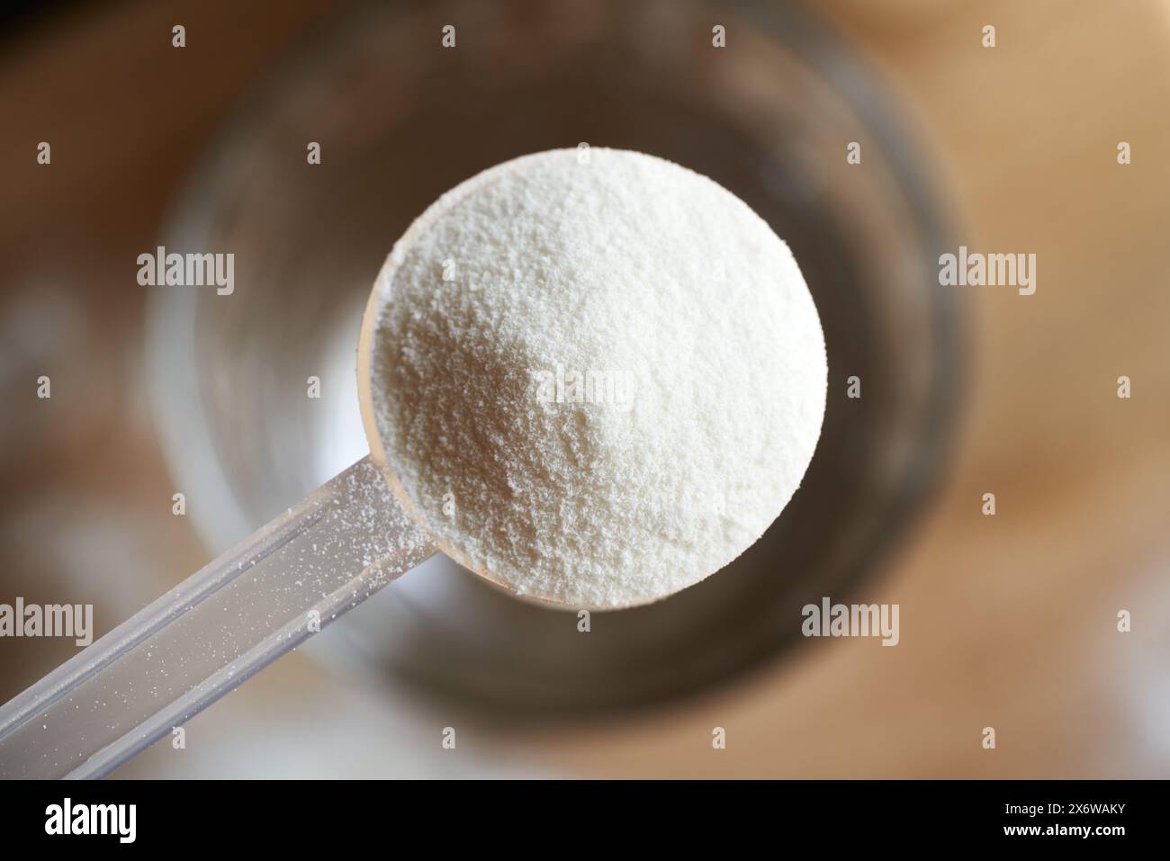 Collagen powder in a plastic measuring spoon above a glass of water ...