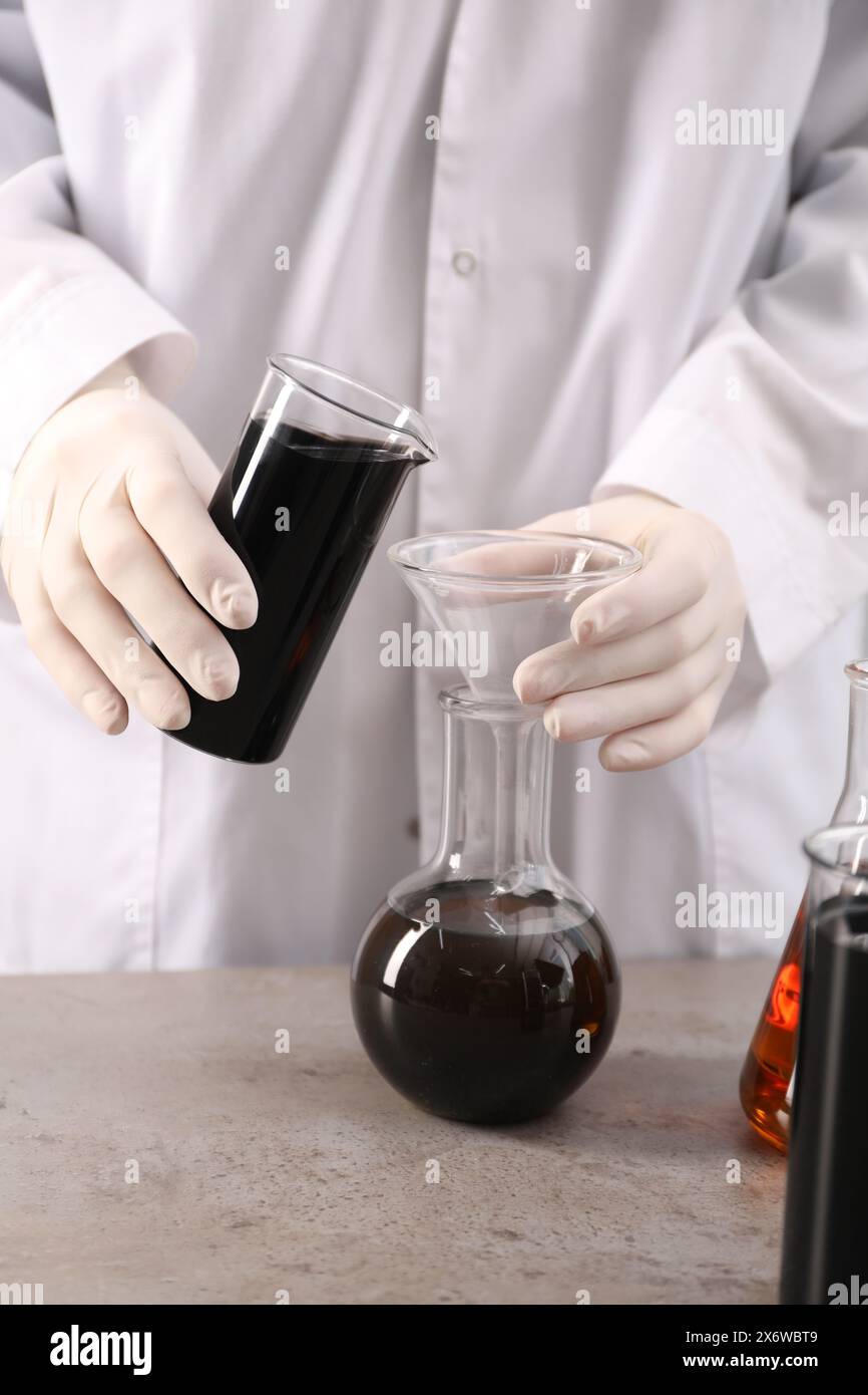 Woman pouring black crude oil from beaker into flask at grey table ...