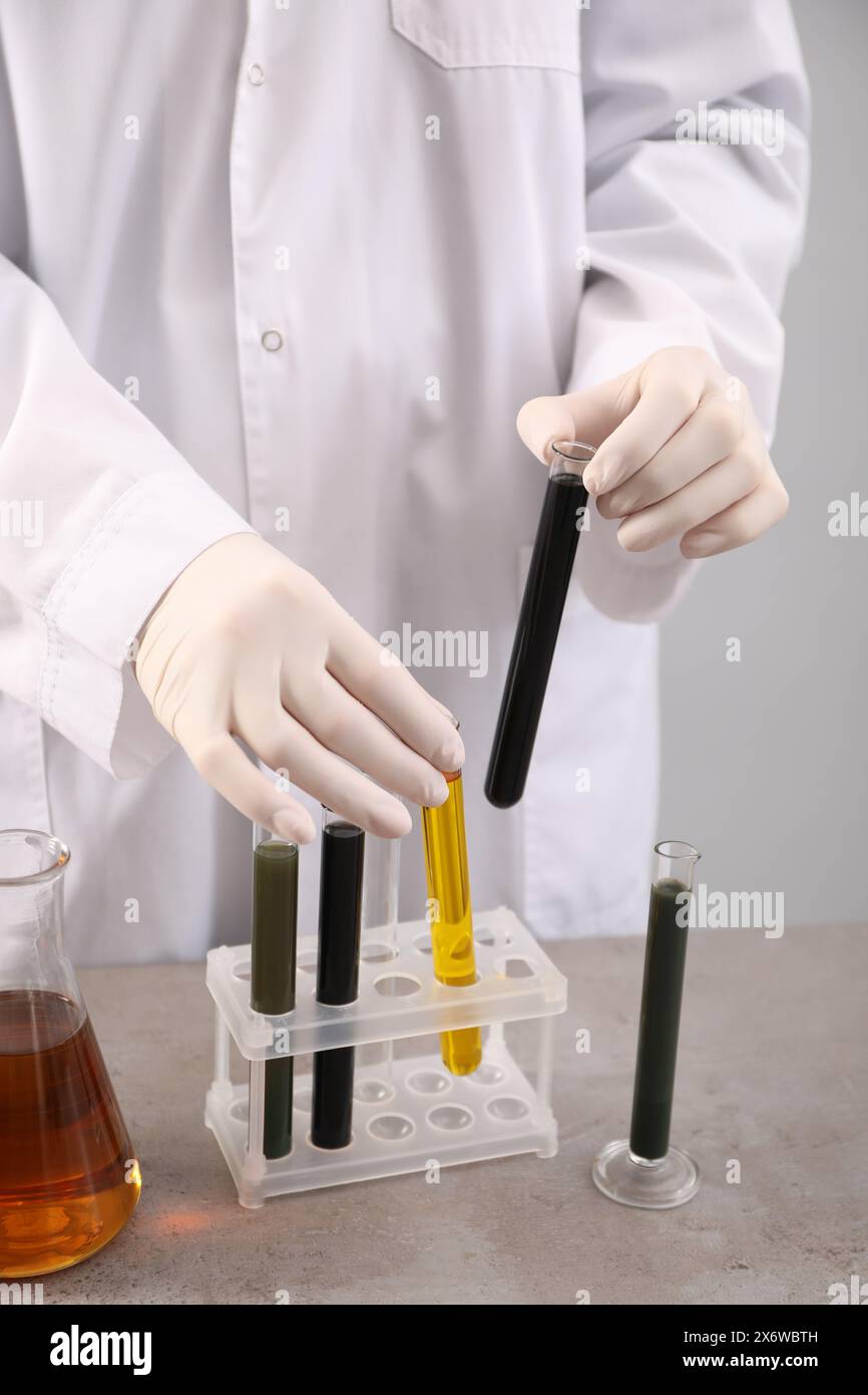 Woman taking test tubes with different types of crude oil from rack at ...