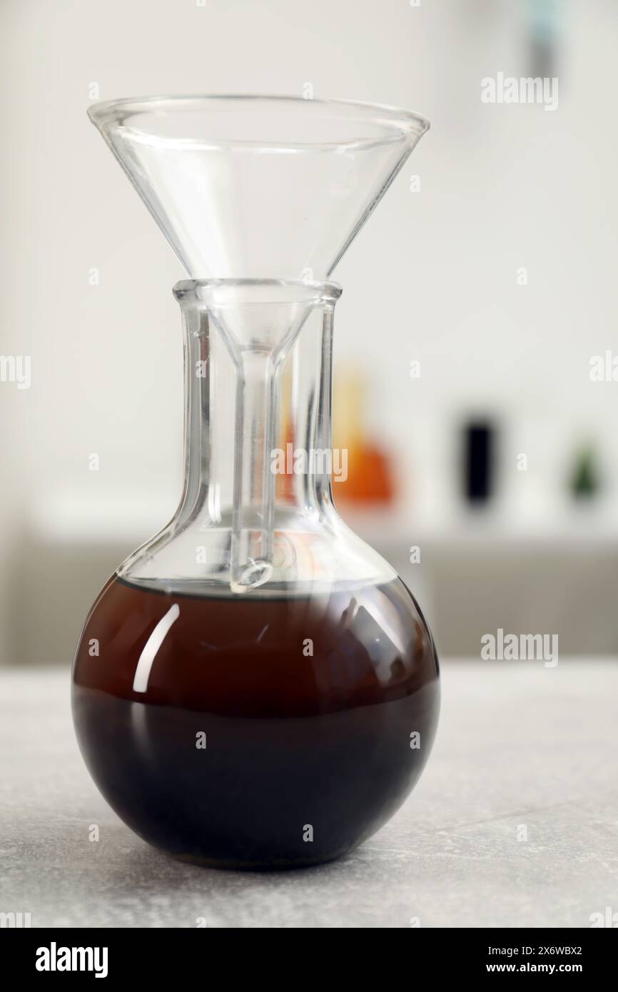 Flask with brown crude oil and filter funnel on light grey table Stock ...