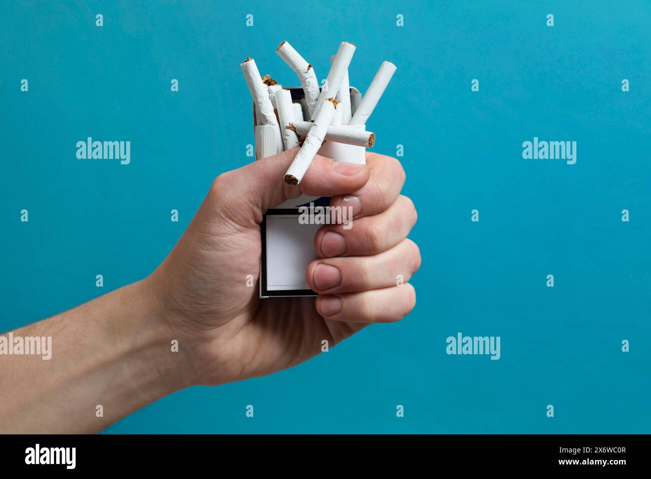 Stop smoking. Man holding pack with broken cigarettes on light blue ...