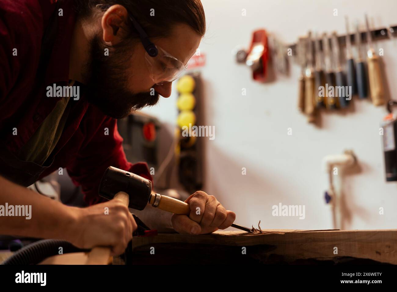 Sculptor shaping raw timber using chisel and hammer in carpentry shop ...