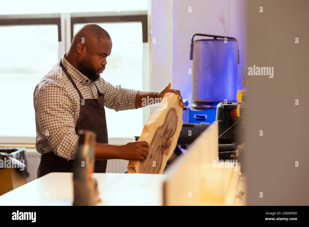 African american carpenter in woodworking shop inspecting wood before ...