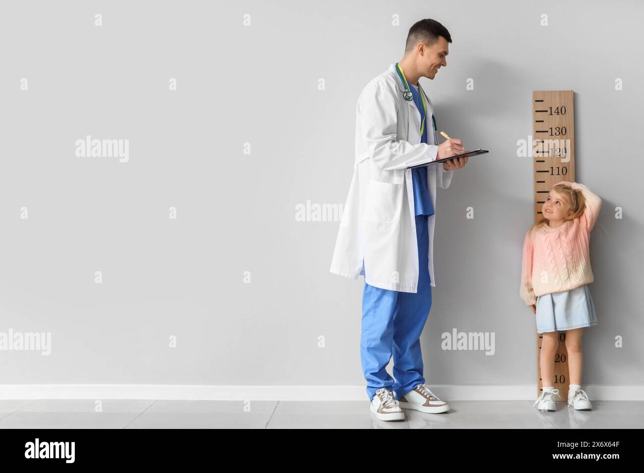 Male pediatrician measuring height of little girl near white wall Stock ...