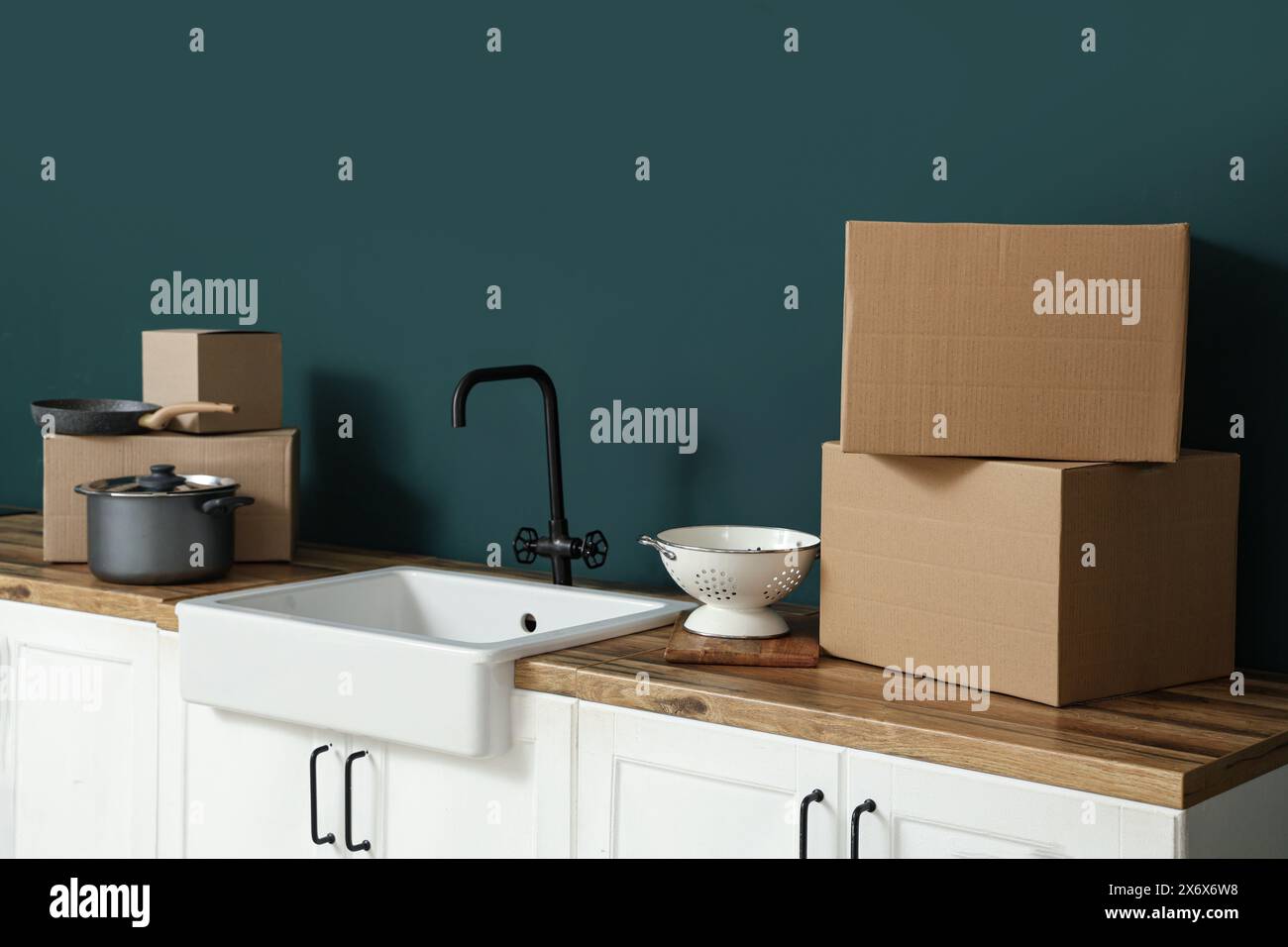 Kitchen counters with cardboard boxes and sink near green wall. Moving ...