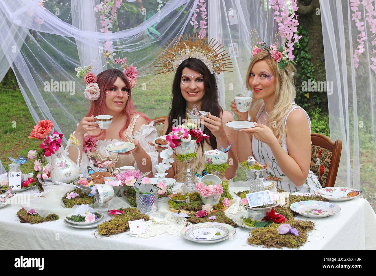 Three women dressed as elves or fairies sit happily at a tea table ...