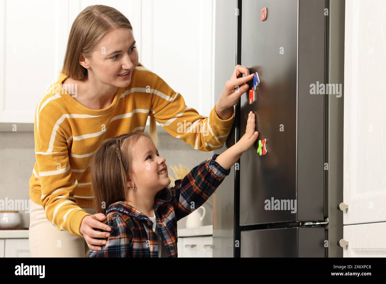 Mom and daughter putting magnetic letters on fridge at home. Learning ...