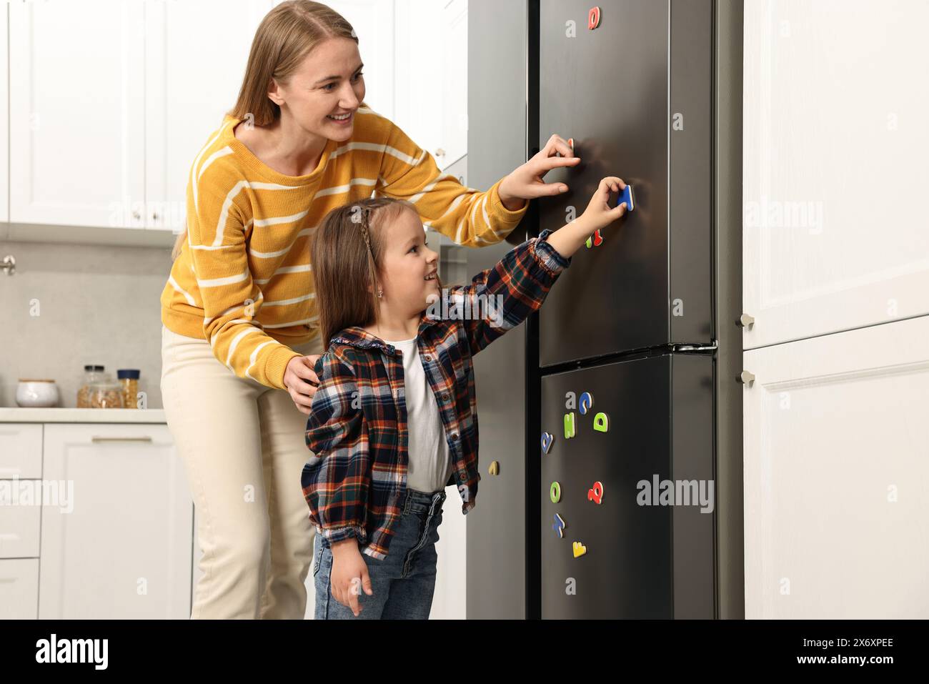 Mom and daughter putting magnetic letters on fridge at home. Learning ...
