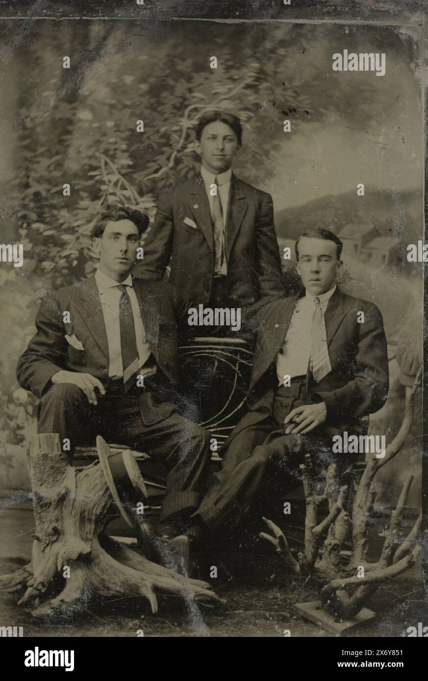 Portrait of three men, two of whom are holding cigars, standing and ...