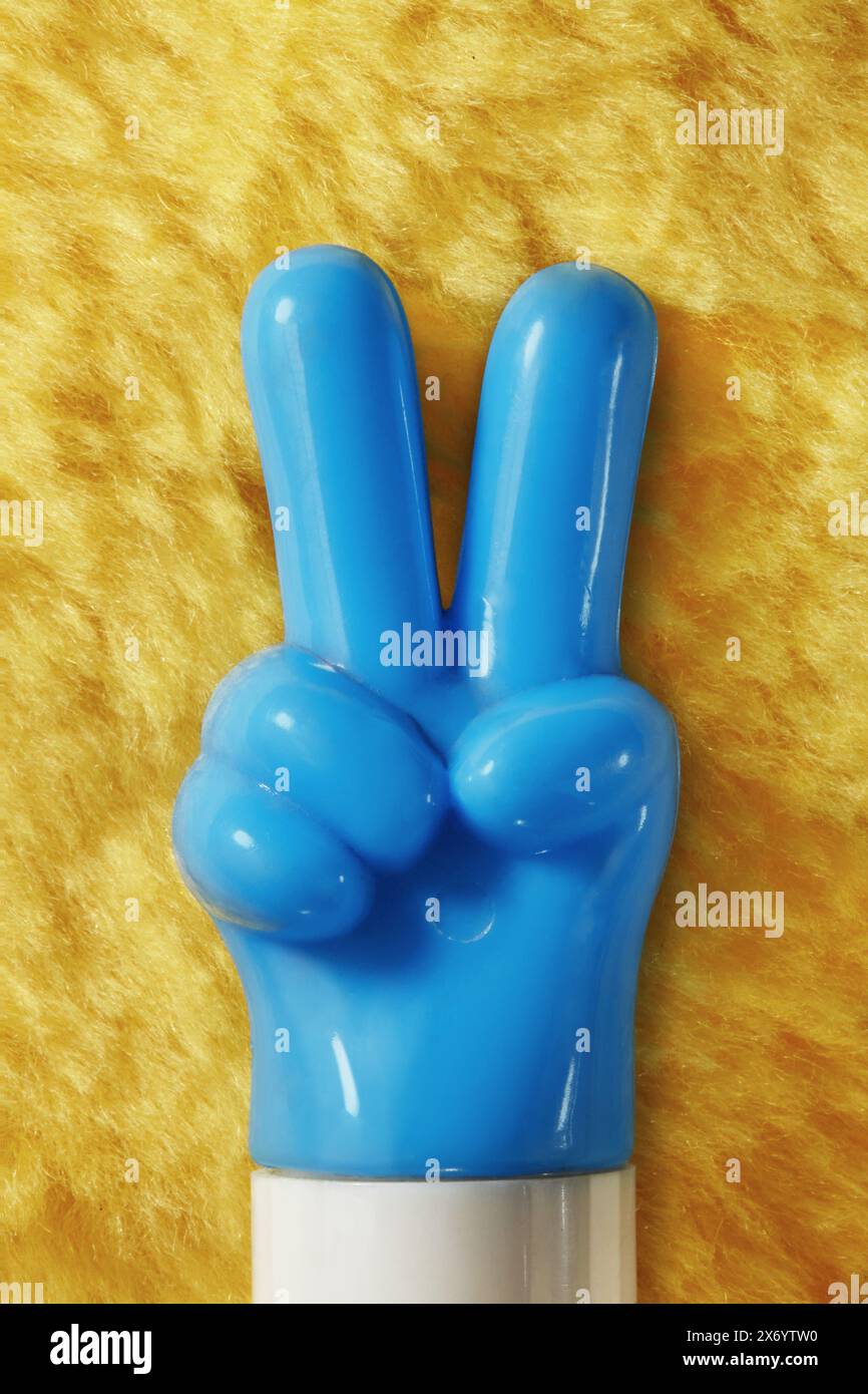 Two finger sign of a blue plastic toy hand on a yellow hairy background ...