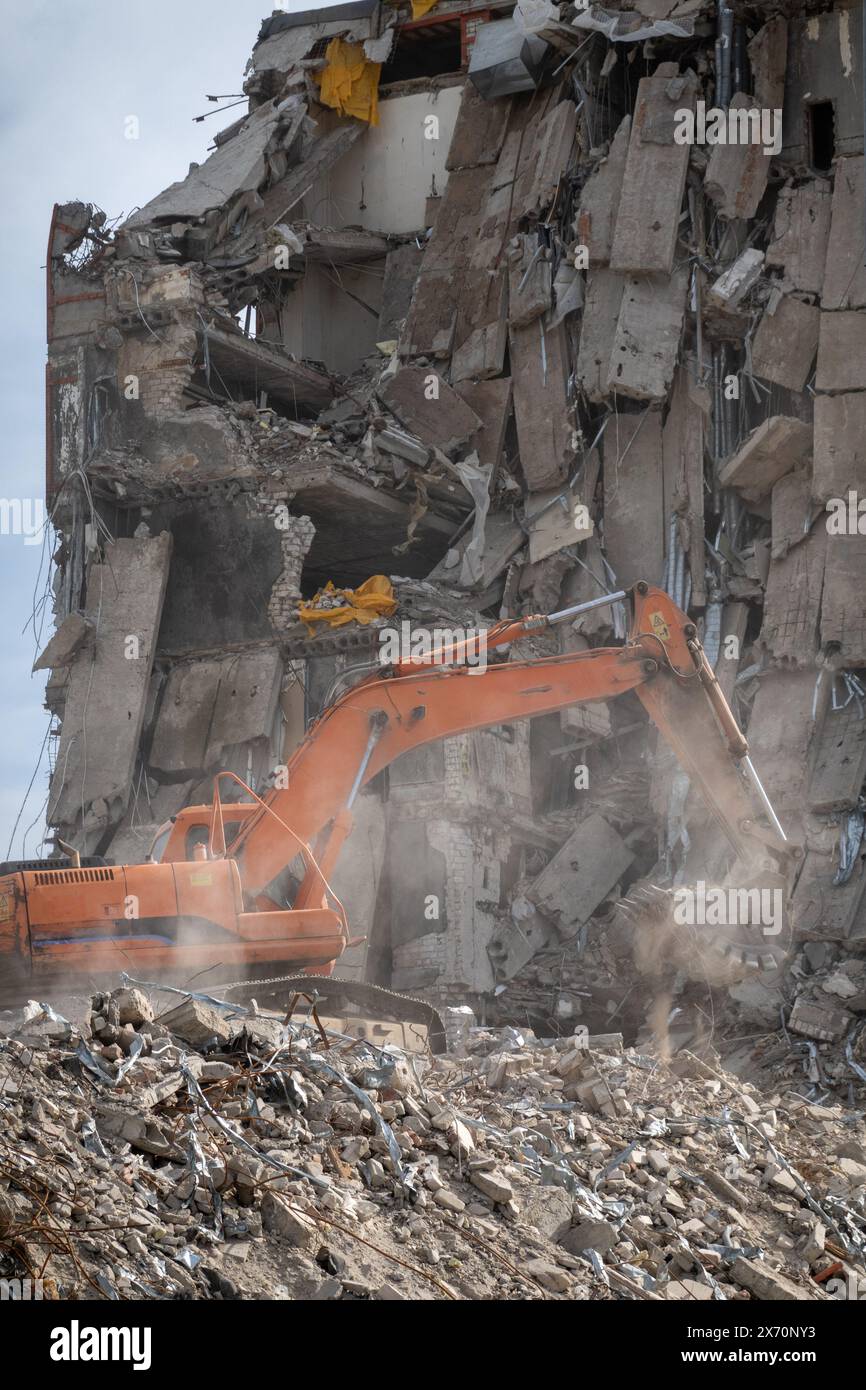 An excavator actively demolishes an old building, creating a scene of ...